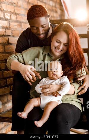 Joyful multiracial parents playing with their child on shoulders in a ...