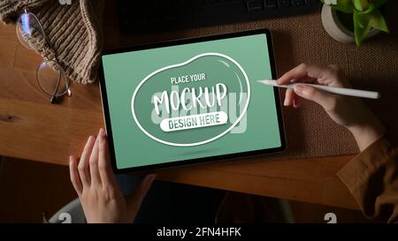 Overhead shot of hands using mock up tablet with stylus pen on dark office desk with laptop and ...