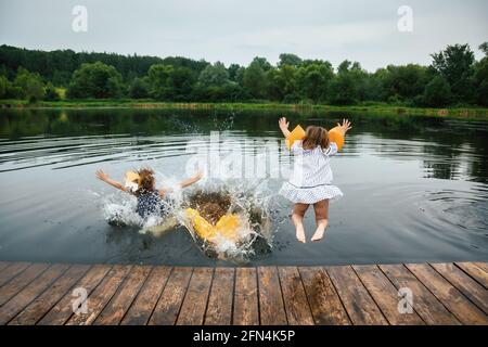 Girls jumping into lake from wooden dock Stock Photo - Alamy