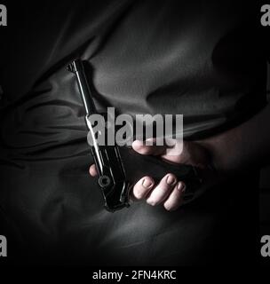 Man holding a loaded gun behind his back Stock Photo - Alamy