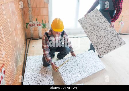 Craftsman measuring tile with ruler with his assistant at construction ...