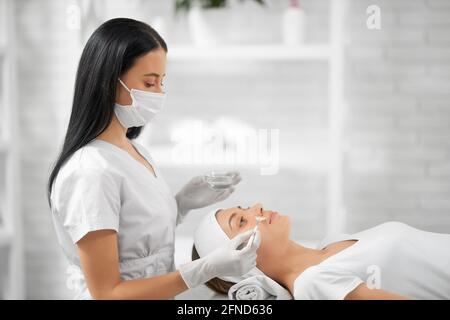 Female aesthetician in protective face mask discussing with woman at ...
