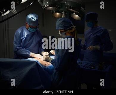 Surgical team doing aesthetic surgery in operating room. Doctors doing ...