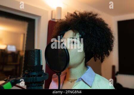 Black female singer performing song against microphone with pop filter ...