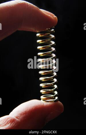 The male hand squeezes a metal spring on a black background Stock Photo ...