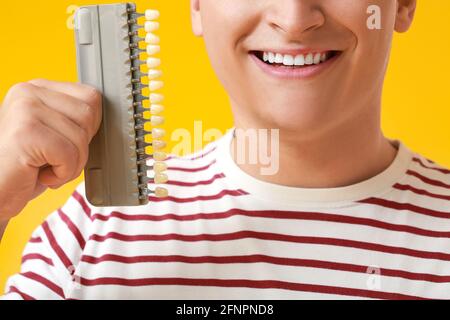 Young man with teeth color chart on yellow background Stock Photo - Alamy
