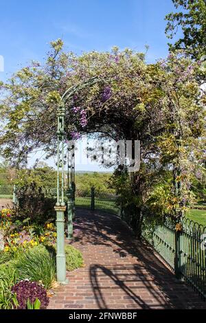 A plant covered arched arbor trellis at the entrance to a picturesque ...