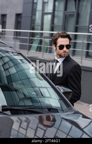 bearded bodyguard in suit and sunglasses with security earpiece sitting ...