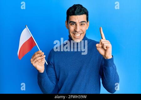 Handsome hispanic man holding poland flag smiling happy and positive ...