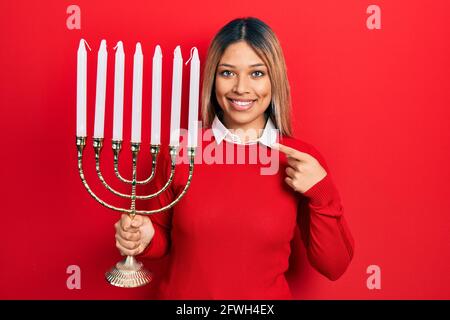 Beautiful hispanic woman holding menorah hanukkah jewish candle looking ...