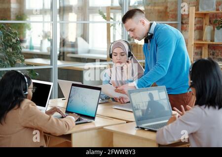 Young manager with script pointing at computer monitor and discussing ...