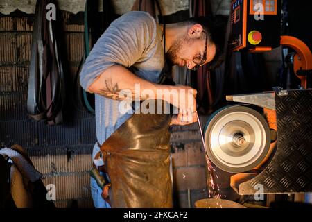 Grinding craftsman sharpening metal at workshop, with grinder, apron ...