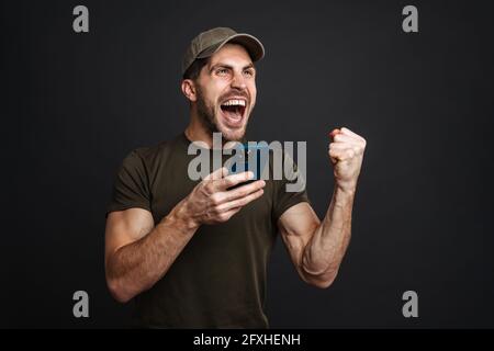 Excited military man making winner gesture while using cellphone ...