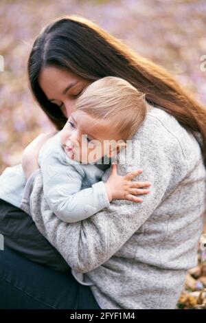 Mom hugs the baby to her chest, sitting on the foliage in the park ...