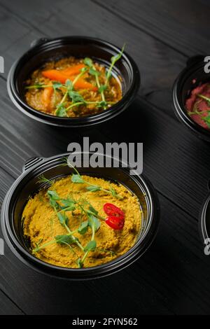 Hummus garnished with peppers and herbs in black plate on dark wooden ...