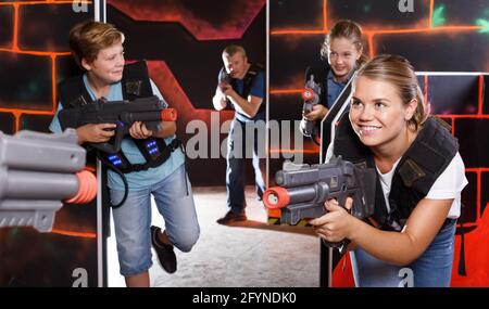 Excited kids and theirs parents aiming laser guns and playing laser tag ...