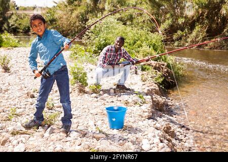 Afro boy holding fishing rod and pulling fish from river Stock Photo ...