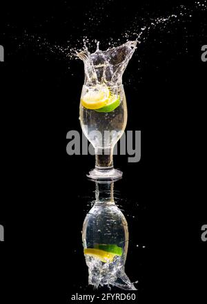 Vertical shot of lemon slices splashing into glass water on isolated black background Stock ...