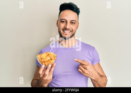 Young arab man holding potato chip celebrating achievement with happy ...