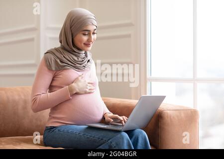 Pregnant Muslim woman sitting on sofa at home Stock Photo - Alamy