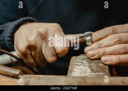 Hands of anonymous male goldsmith using manual tool to shape metal ring ...