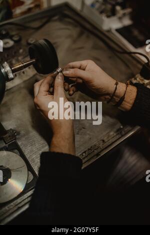 Hands of anonymous male goldsmith using manual tool to shape metal ring ...