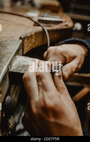 Hands of anonymous male goldsmith using manual tool to shape metal ring ...
