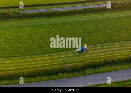 a farmer tends to his field in a tractor while a Circus sets up next to ...