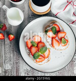 Two toasts with strawberry, mint, cup of coffee on wooden table ...