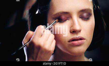 Makeup artist applying eye shadow to the lower eyelid of a girl with a ...