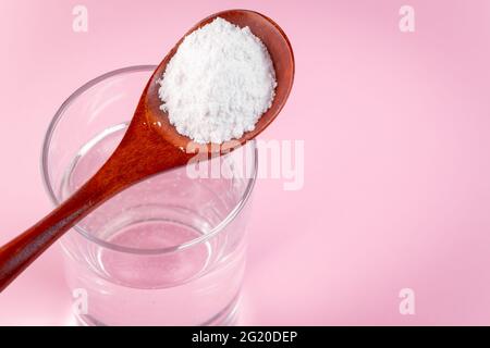 Collagen powder in spoon on glass of water on light gray background ...