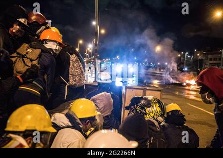 Demonstrators take cover behind a homemade shield in front of a riot ...