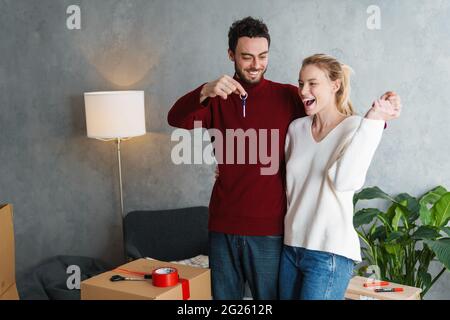 Happy young couple with key from their new house and boxes sitting on ...