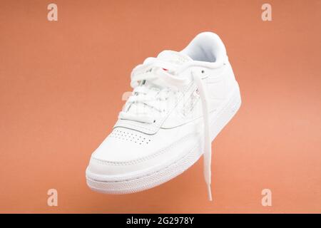 Levitation of single female stylish white casual sneaker on brown ...