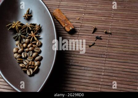 Brown canoe-shaped dish on bamboo mat with coffee beans, star anise ...