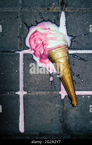 Fallen ice cream cone with spilled pink ice cream on a textured ...