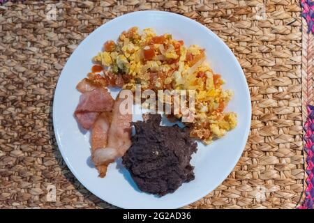 Mexican-style eggs, bacon, and refried beans on a white plate Stock ...