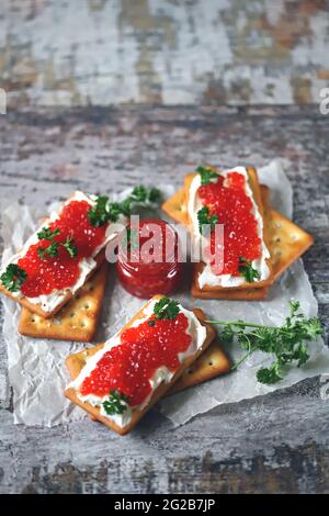 Tasty crackers with cheese and red caviar on light wooden background ...