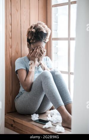 An African female with thinking face sitting with phone and notebook in ...