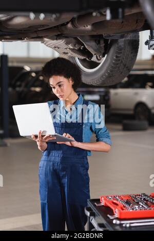 young african american mechanic typing on laptop in garage Stock Photo ...