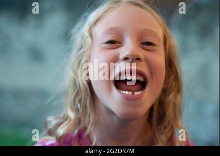 A young girl proudly shows off her mouth and the gap in her teeth where ...