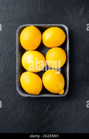 Ripe lemons set, in plastic tray, on black background, top view flat ...