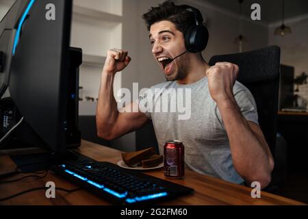 Excited guy in headphones making winner gesture while playing video ...