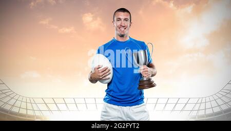 Composition of male rugby player celebrating victory, holding trophy at ...