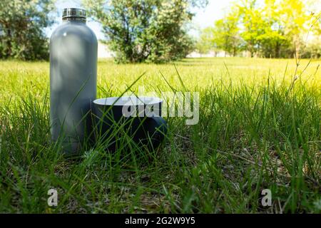 Thermos and a mug in the grass. Camping. A mug with tea in a green ...