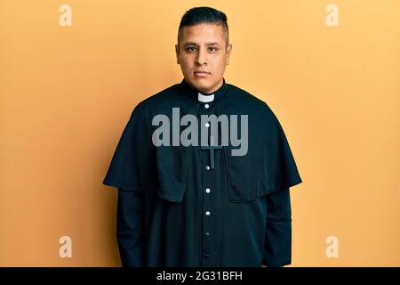 Young latin priest man standing over yellow background clapping and ...
