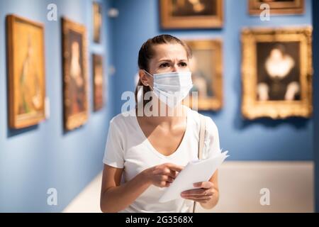 Woman in mask observing artworks in museum Stock Photo - Alamy