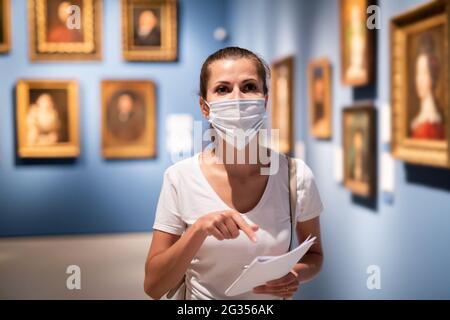 Woman in mask observing artworks in museum Stock Photo - Alamy
