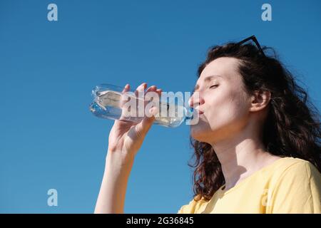 Girl drinks from a bottle in the street. A teenage girl in headphones ...