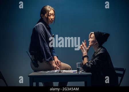 A female investigator sits on a table and interrogates a young criminal ...